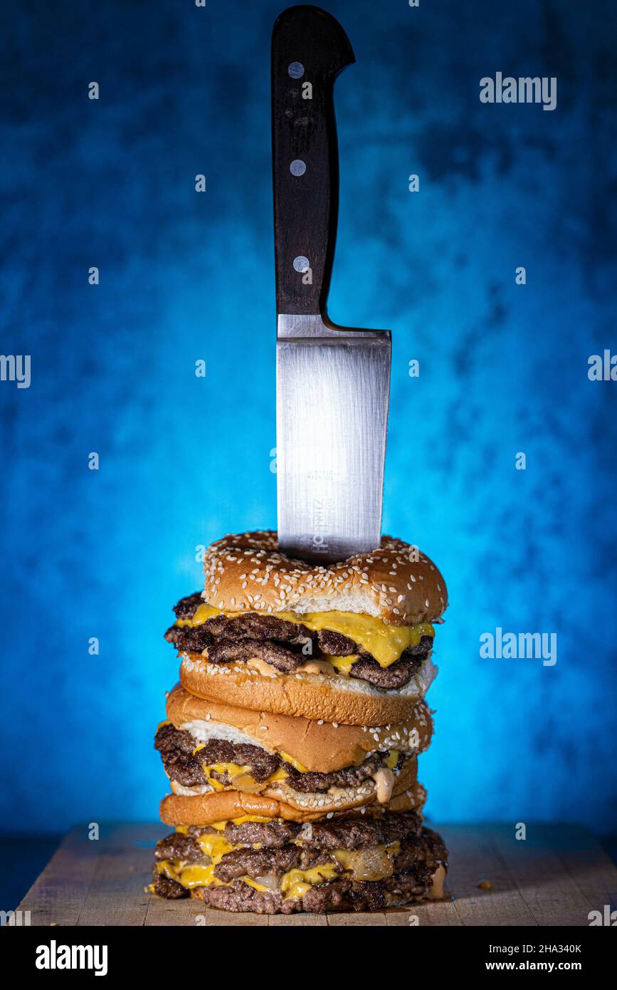 Vertical shot of a stack of gourmet burgers with a knife through them ...