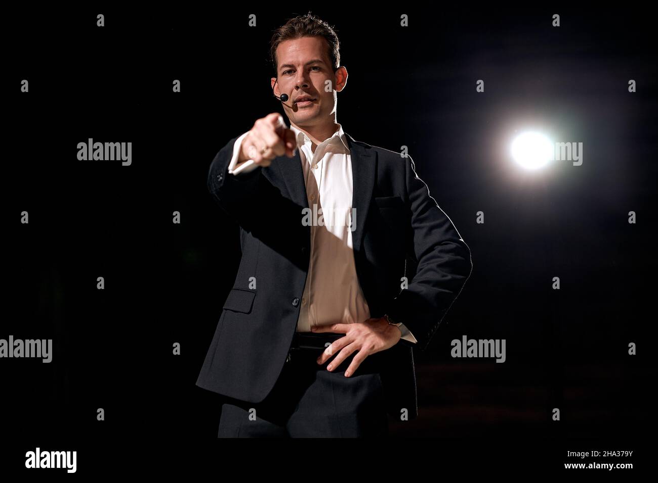 speaker with microphone pointing finger to the listener, standing on ...