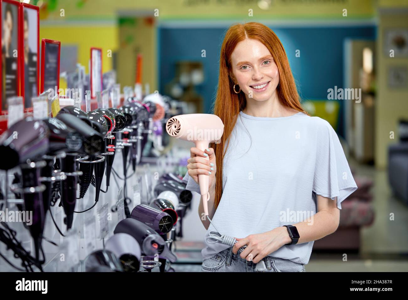 Caucasian redhead woman with long hair, holding hair dryer. Female is ...