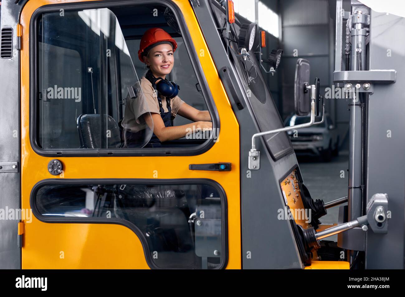 Female worker driving loader in industrial container warehouse, looking ...