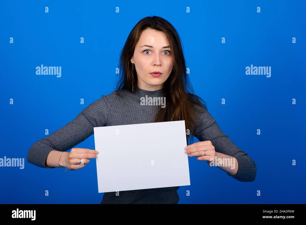 Young woman in grey shirt holding a sheet of paper and looking at the ...