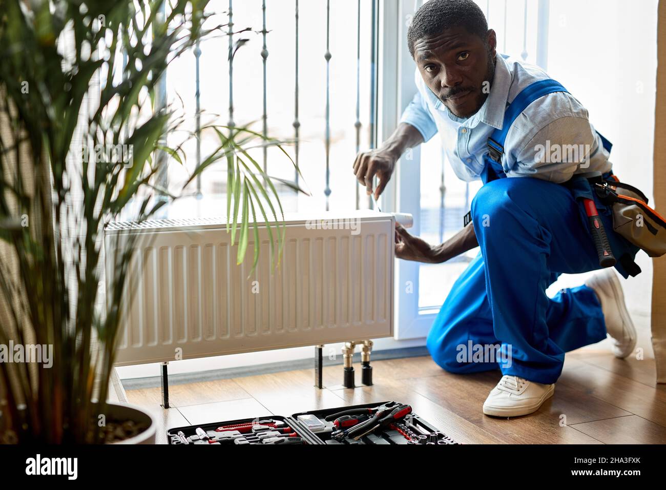 Man in workwear overalls using tools while repairing heating radiator ...