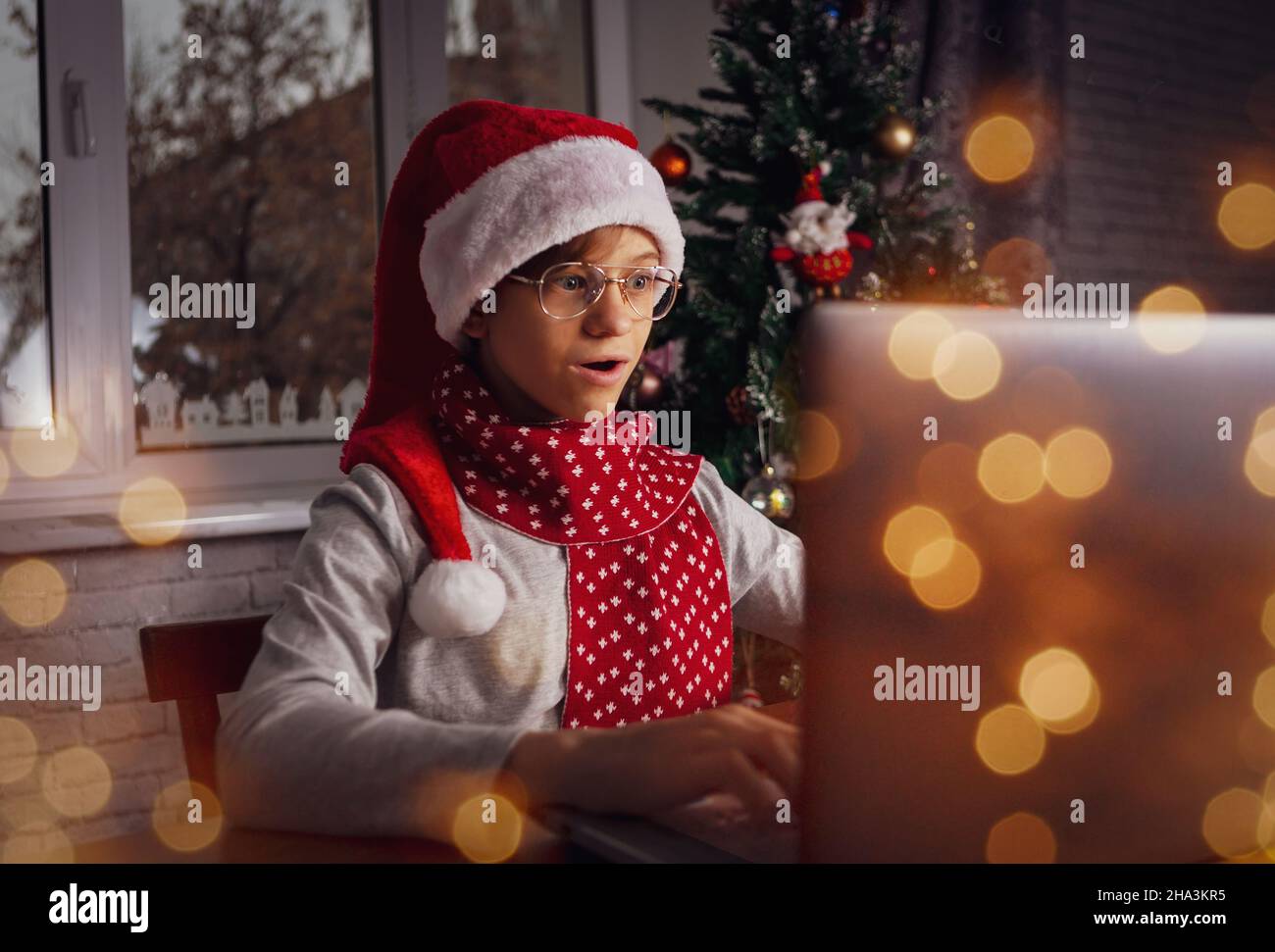 A wondering boy sitting in front of laptop screen wearing red Santa ...