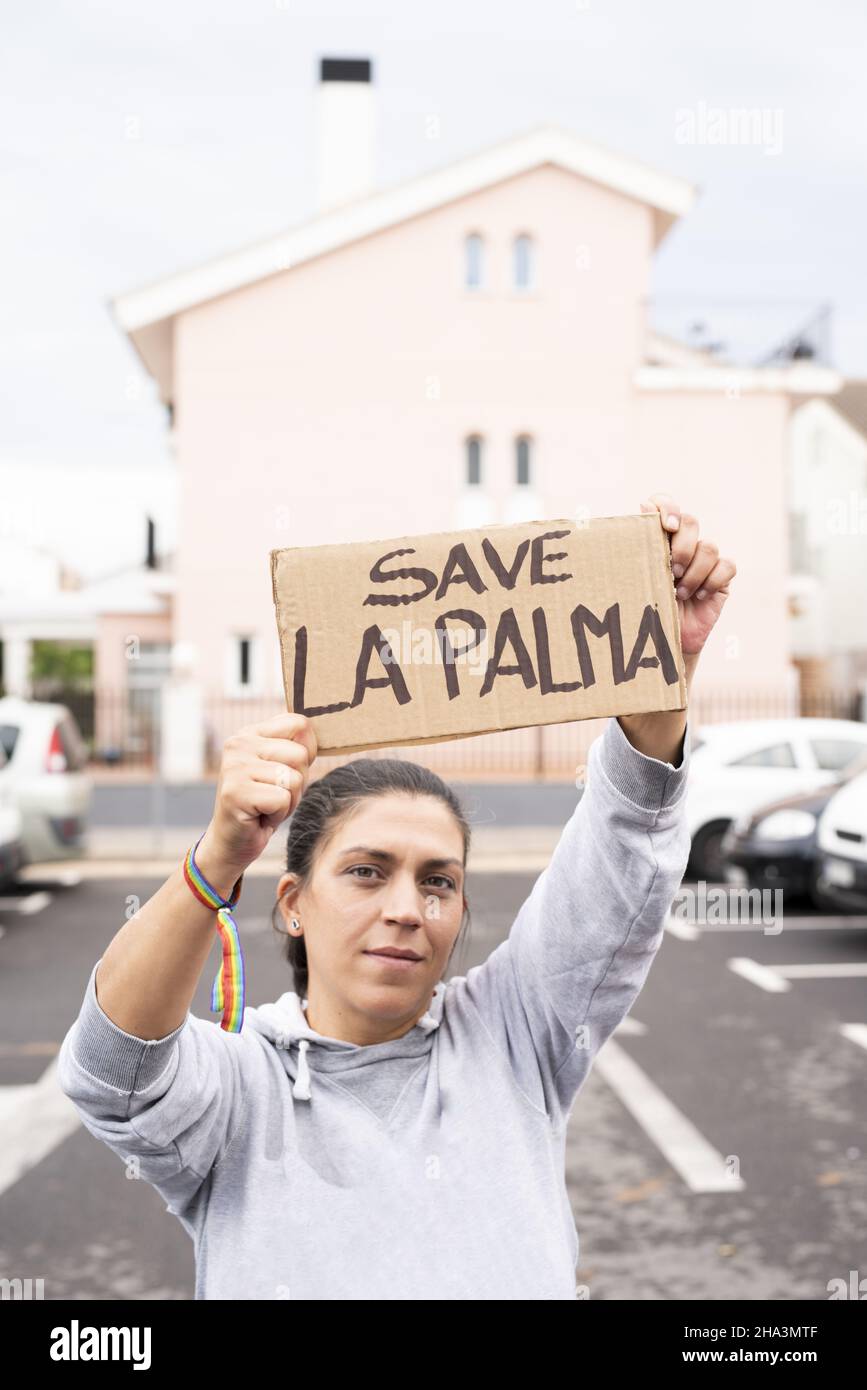 Vertical shot of a "Save La Palma" sign shown by a young Spanish woman ...