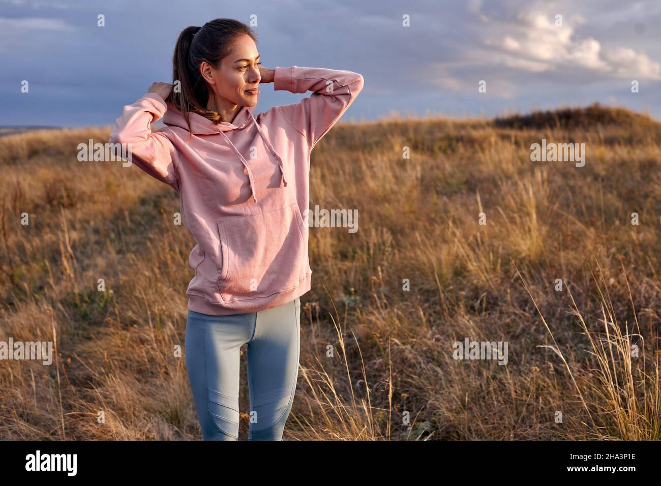 Enthusiastic lady is wearing hoodie hood looking at side at sunset or ...