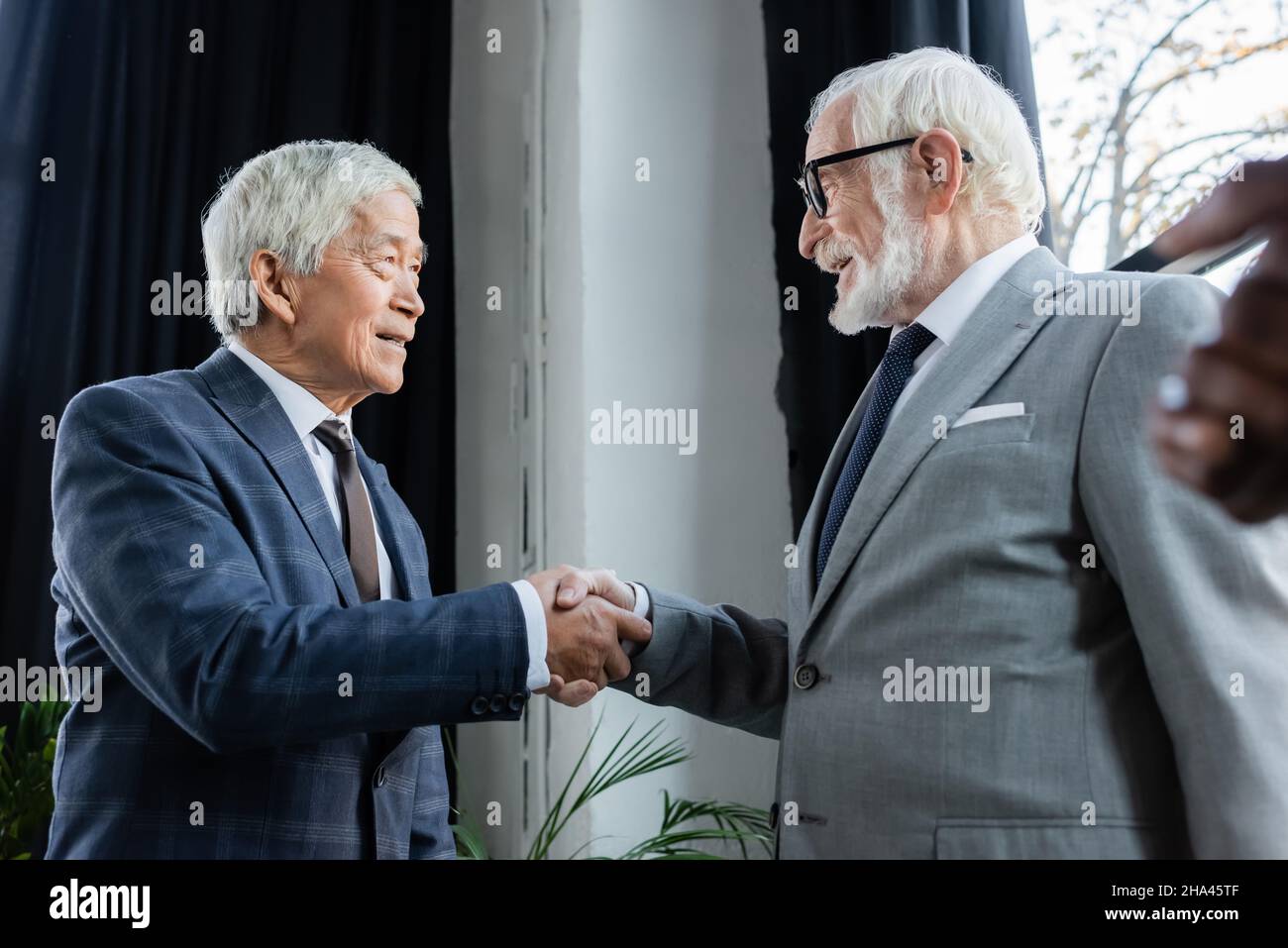 senior interracial business partners smiling while shaking hands in ...