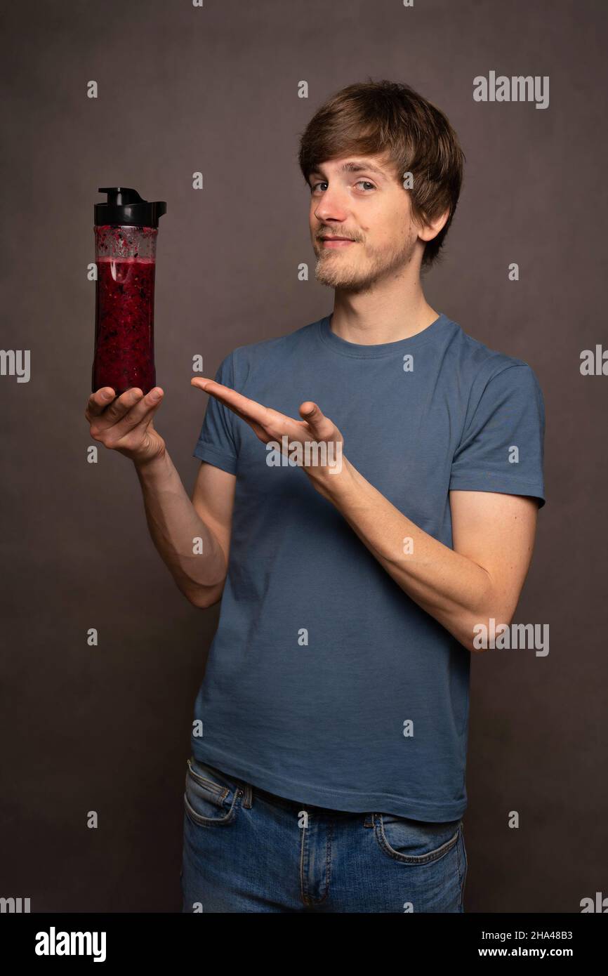 Young handsome tall slim white man with brown hair presenting smoothie ...