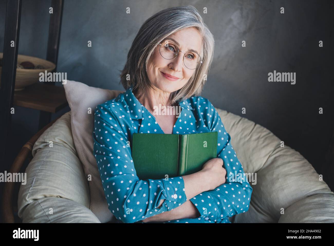 Photo of cheerful nice old lady hug book sit wear blue shirt at home ...