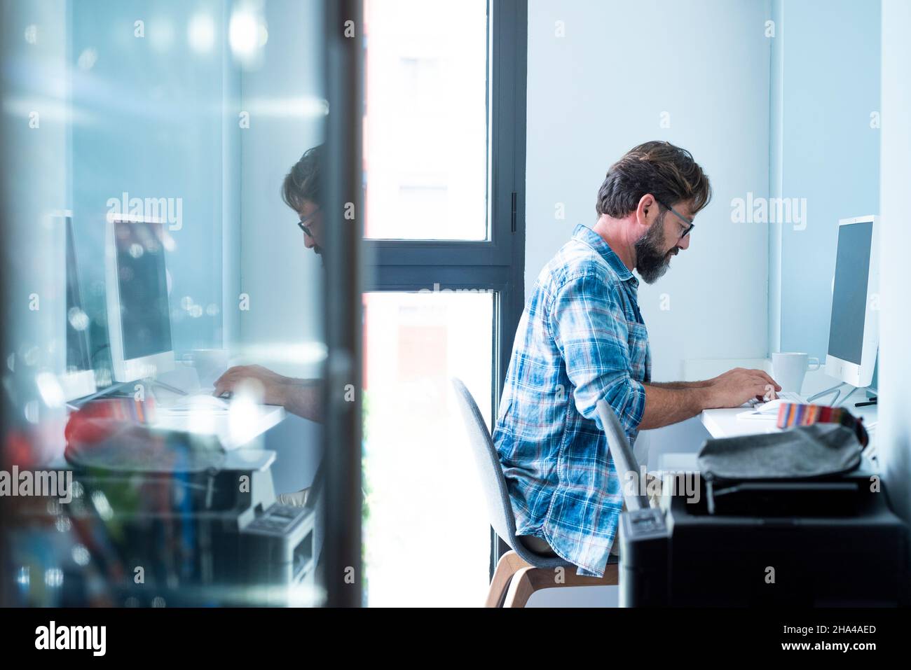 mature man sitting on chair in front of computer and typing on keyboard ...