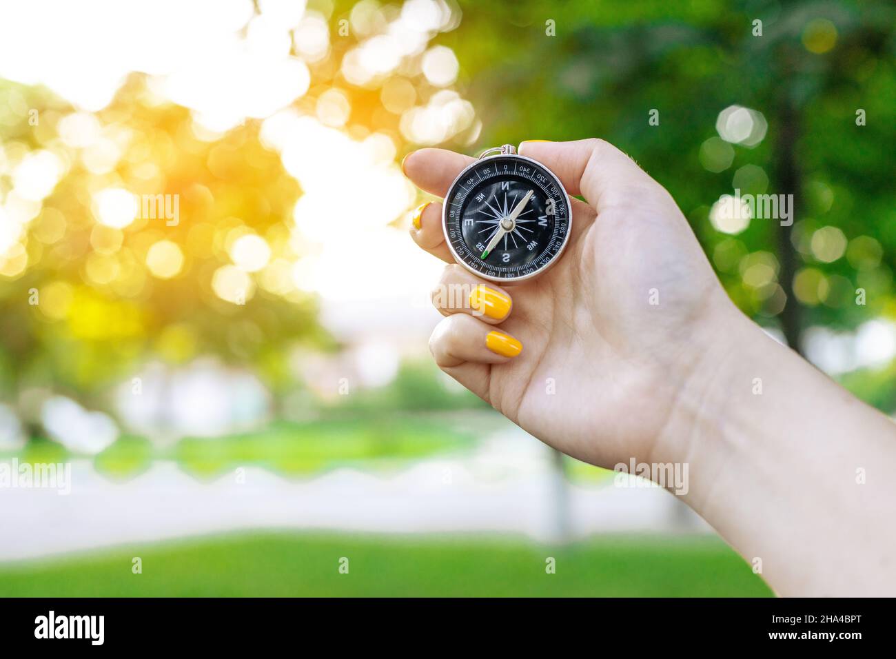 Hand with compass on green blurred background with sun glare at sunset ...