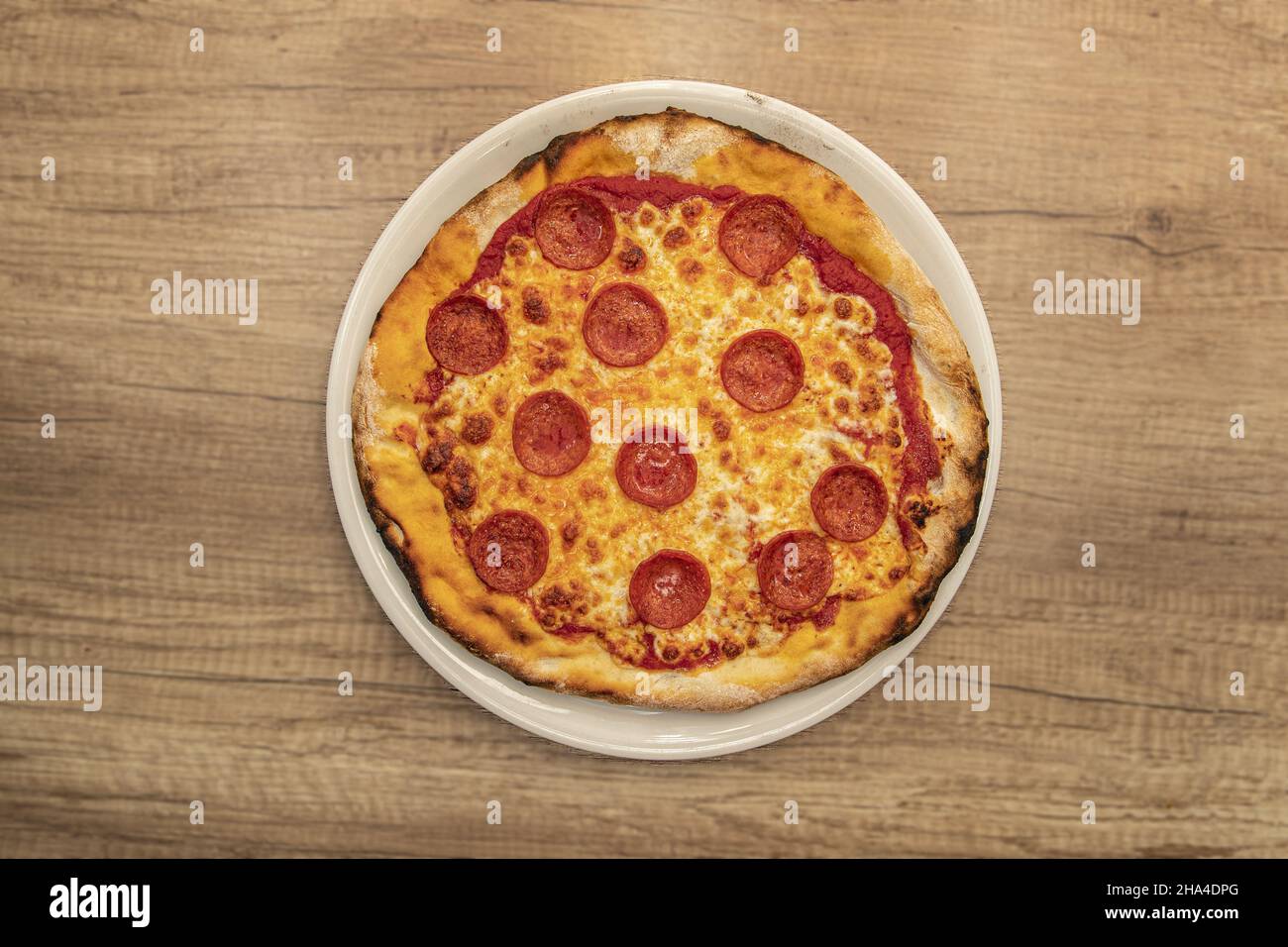 Top view of a tasty Peperoni pizza in a white plate on a wooden table ...