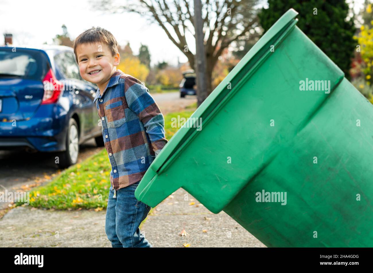 Happy boy pulling green trash can to street Stock Photo - Alamy