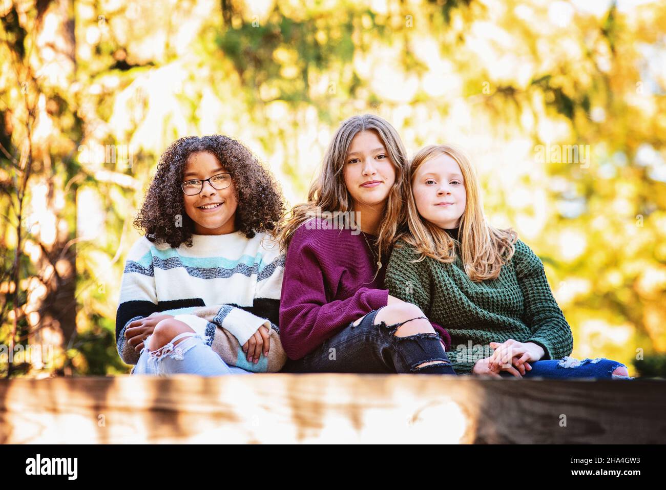 Three pretty tween girls laughing together outdoors in fall colors ...