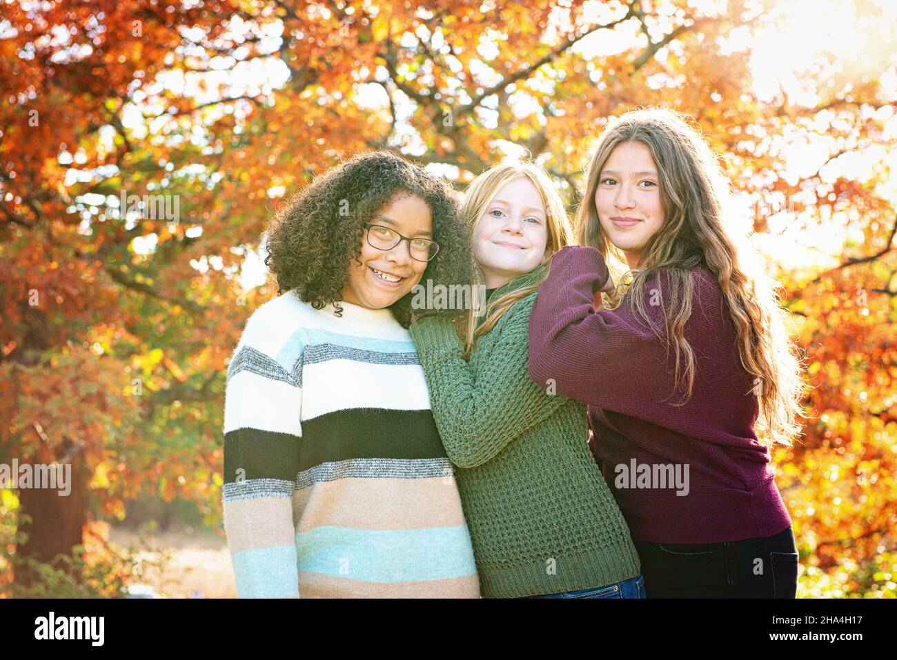 Three pretty tween girls laughing together outdoors in fall colors ...