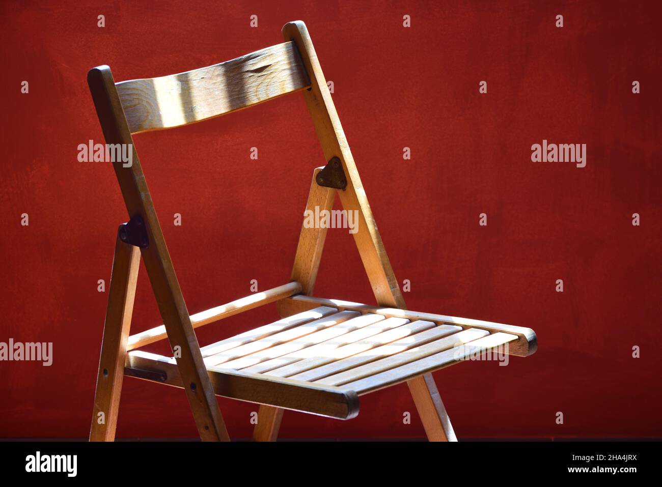 An empty old folding chair made of wood stands in front of a red ...