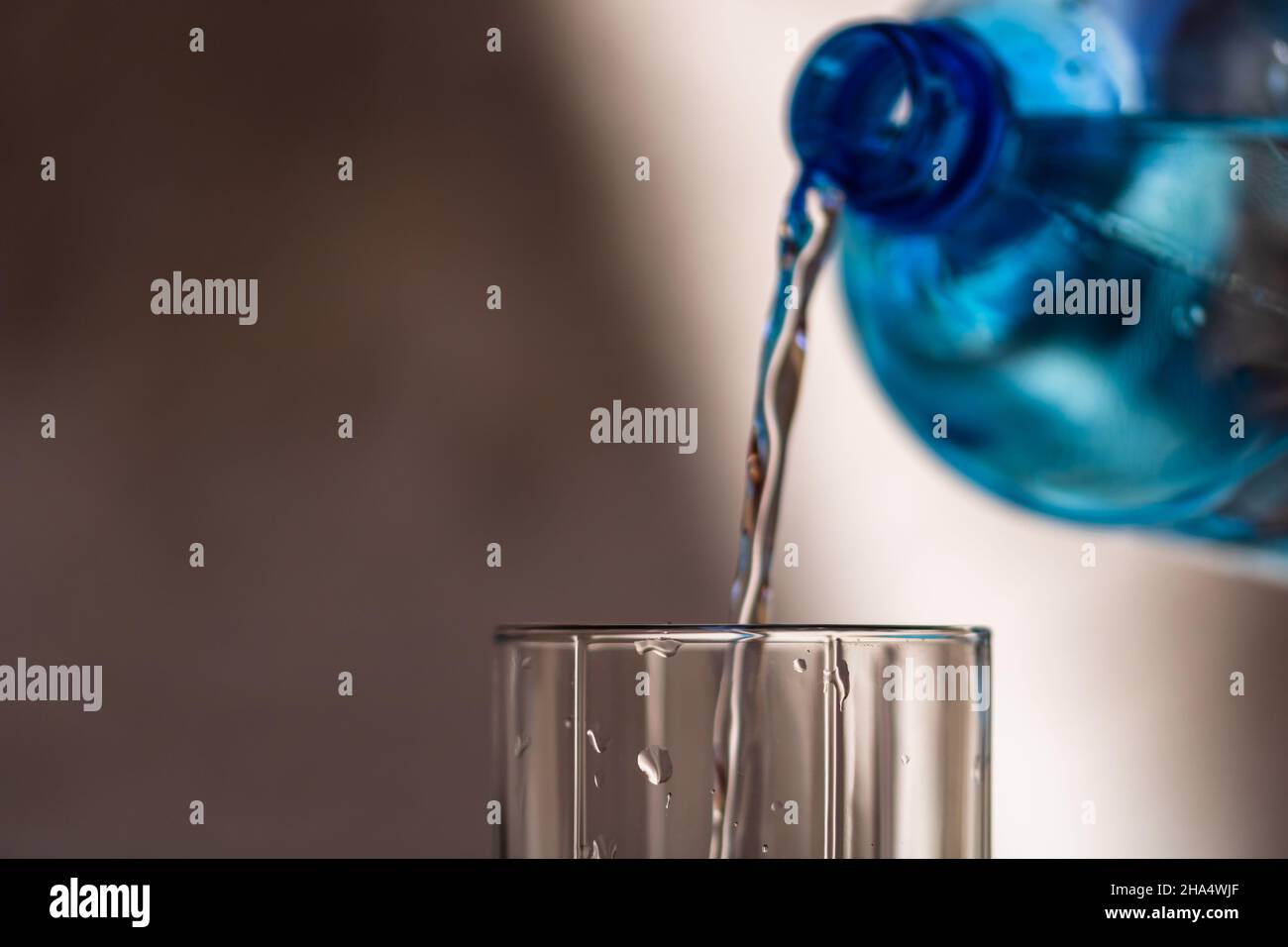 Pouring water from blue plastic bottle into a glass on blurred ...