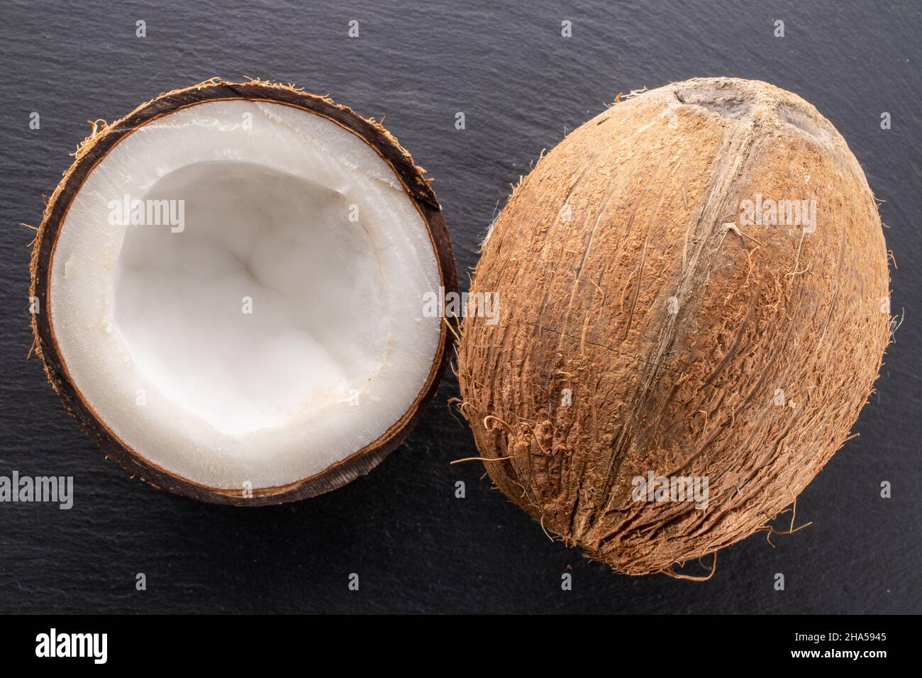 One whole and one half of a fresh coconut, close-up, on a slate board ...