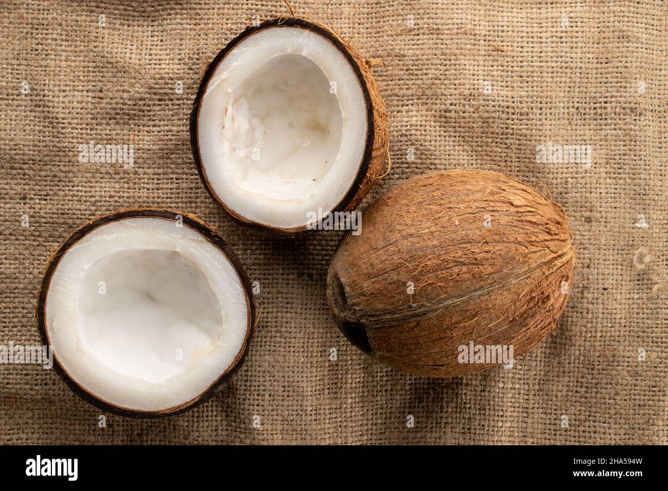 One whole and two halves of fresh coconut, close-up, on sacking, top ...