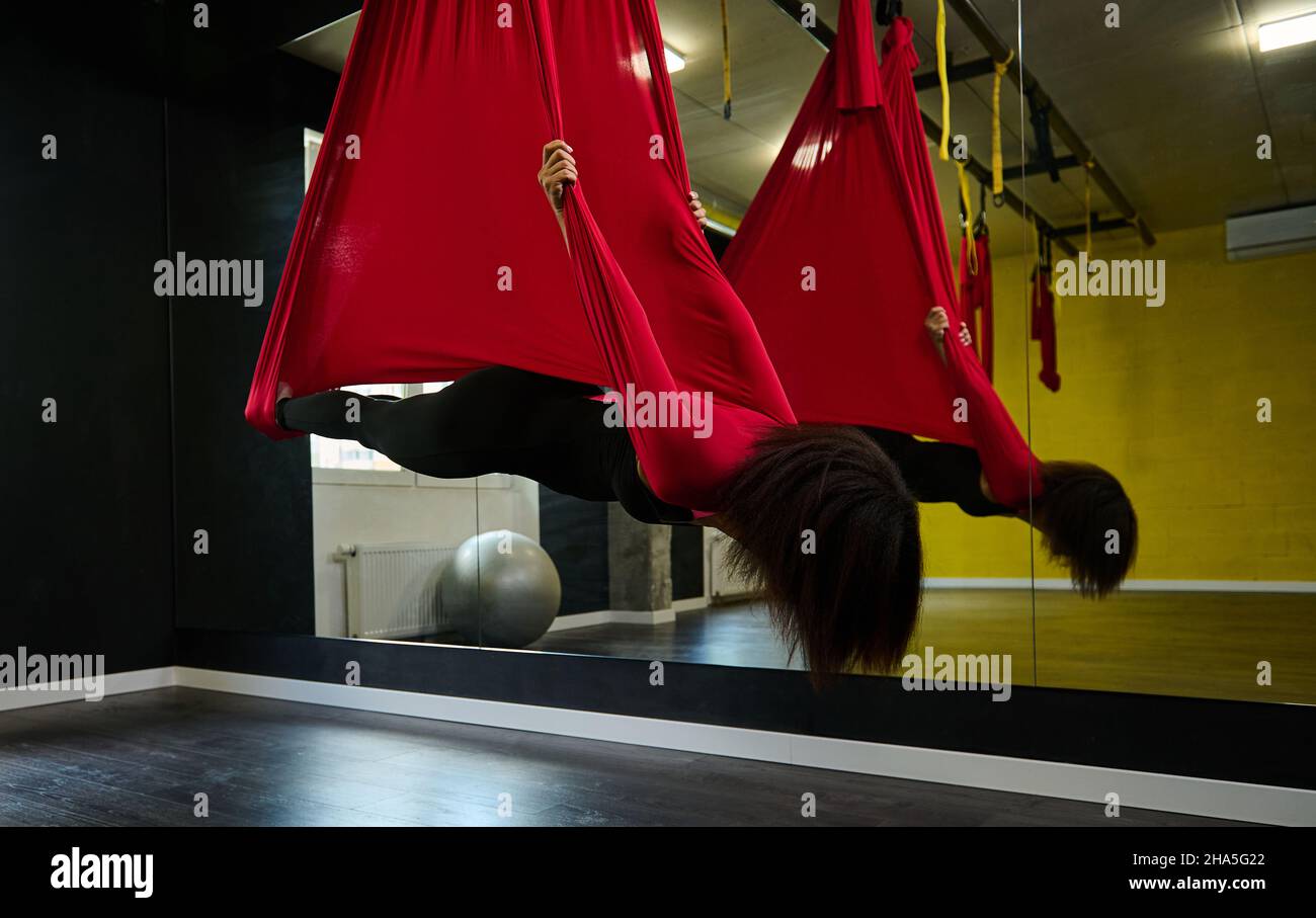 Young sporty African slim body woman practicing aerial flying yoga ...