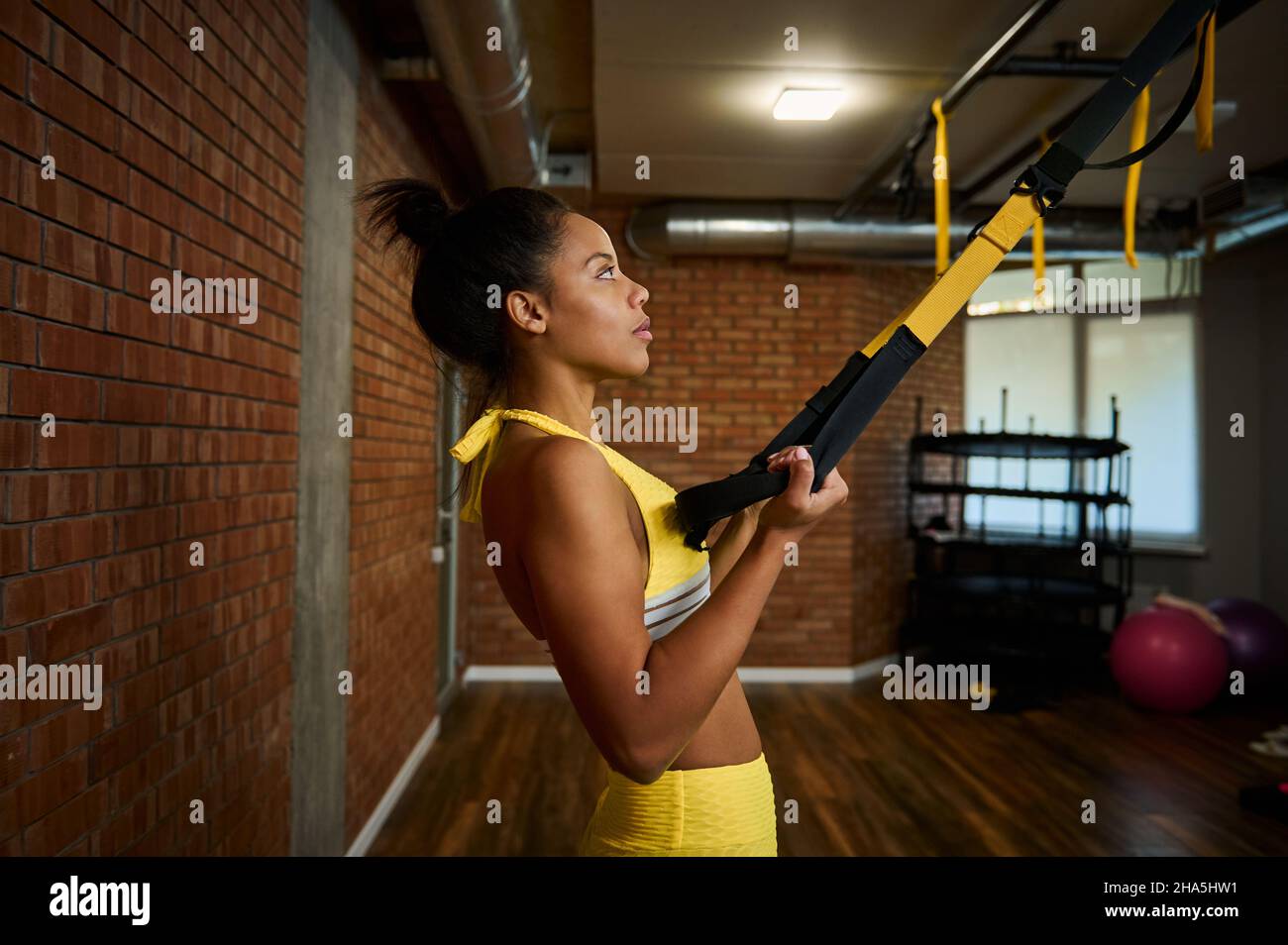 Beautiful African woman doing arm exercises with suspension straps at ...