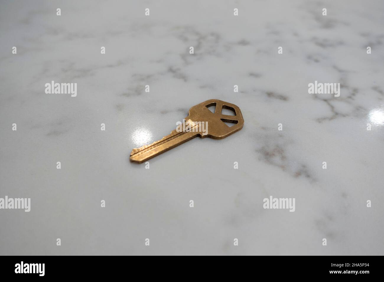 Angled view of a plain, bronze colored key on top of a white marble ...