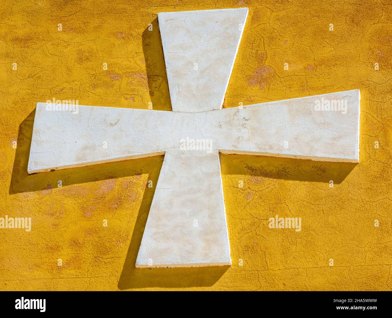 white coloured maltese cross close-up on a yellow painted background on ...