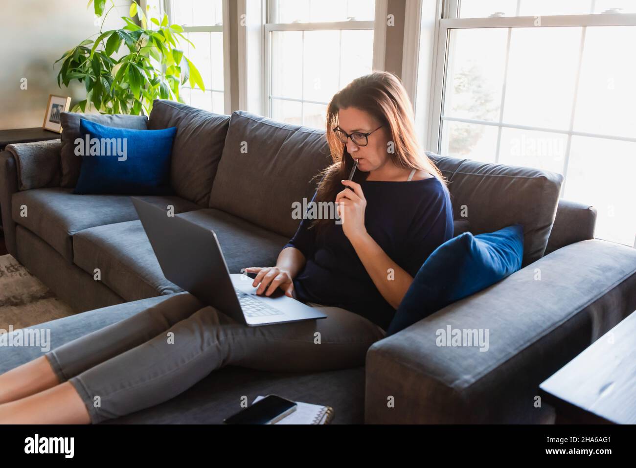 Woman sitting on sofa in living room working on computer Stock Photo ...