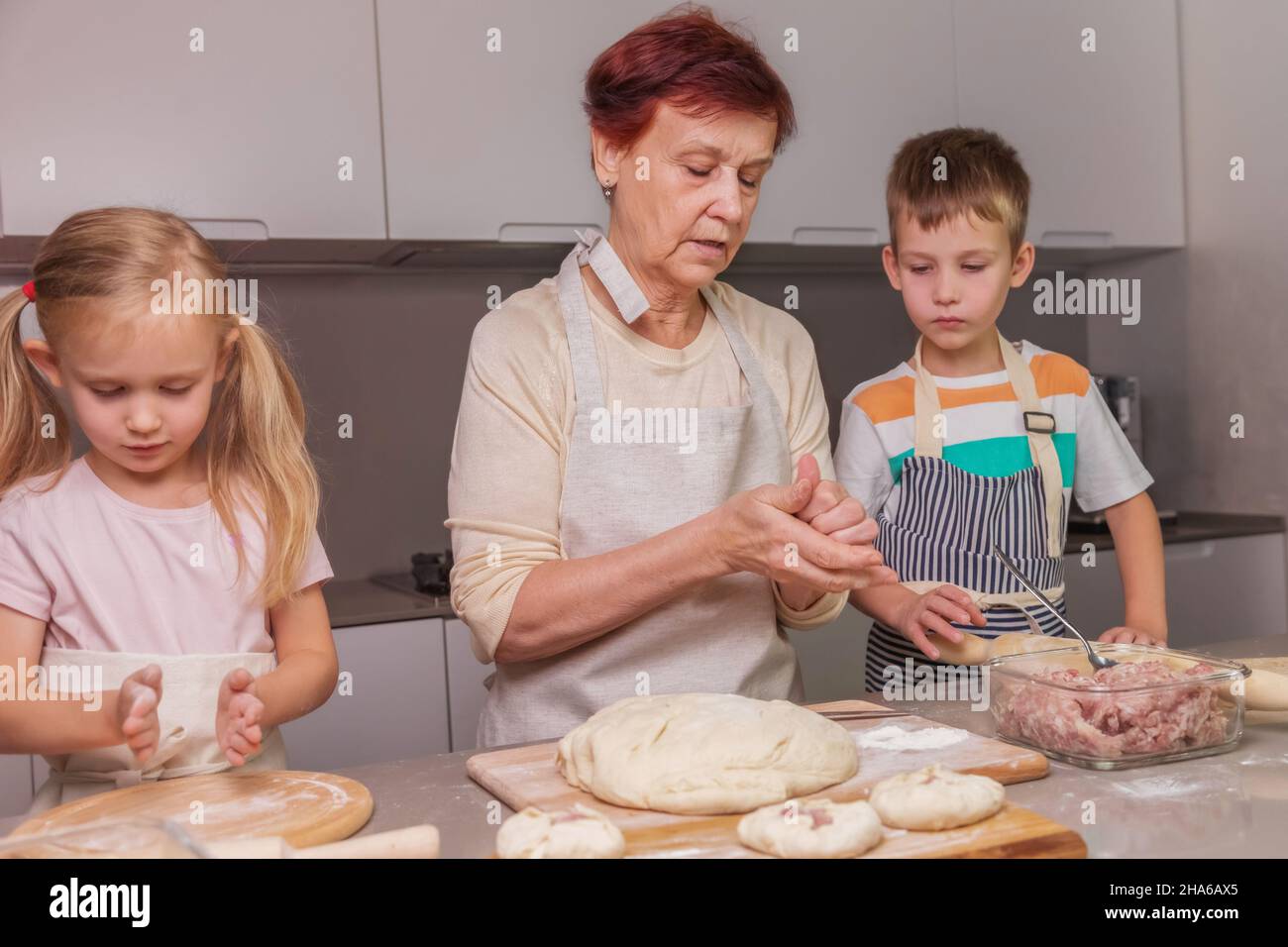 Grandma shows the twins how to cook a traditional meat dish Stock Photo ...