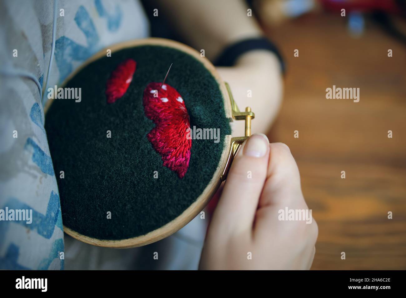 Female is embroidering mushroom cap on green cloth. Girl sewing floss ...