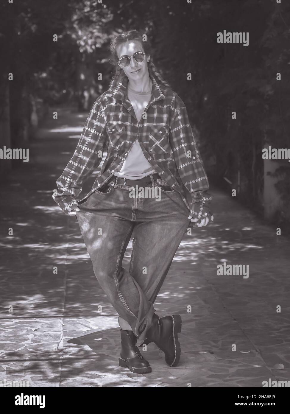 A girl with pigtails in a plaid shirt and very wide jeans stands in ...