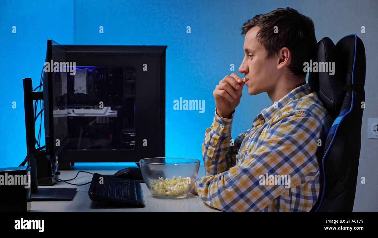Young man watches stream with computer and eats popcorn Stock Photo - Alamy