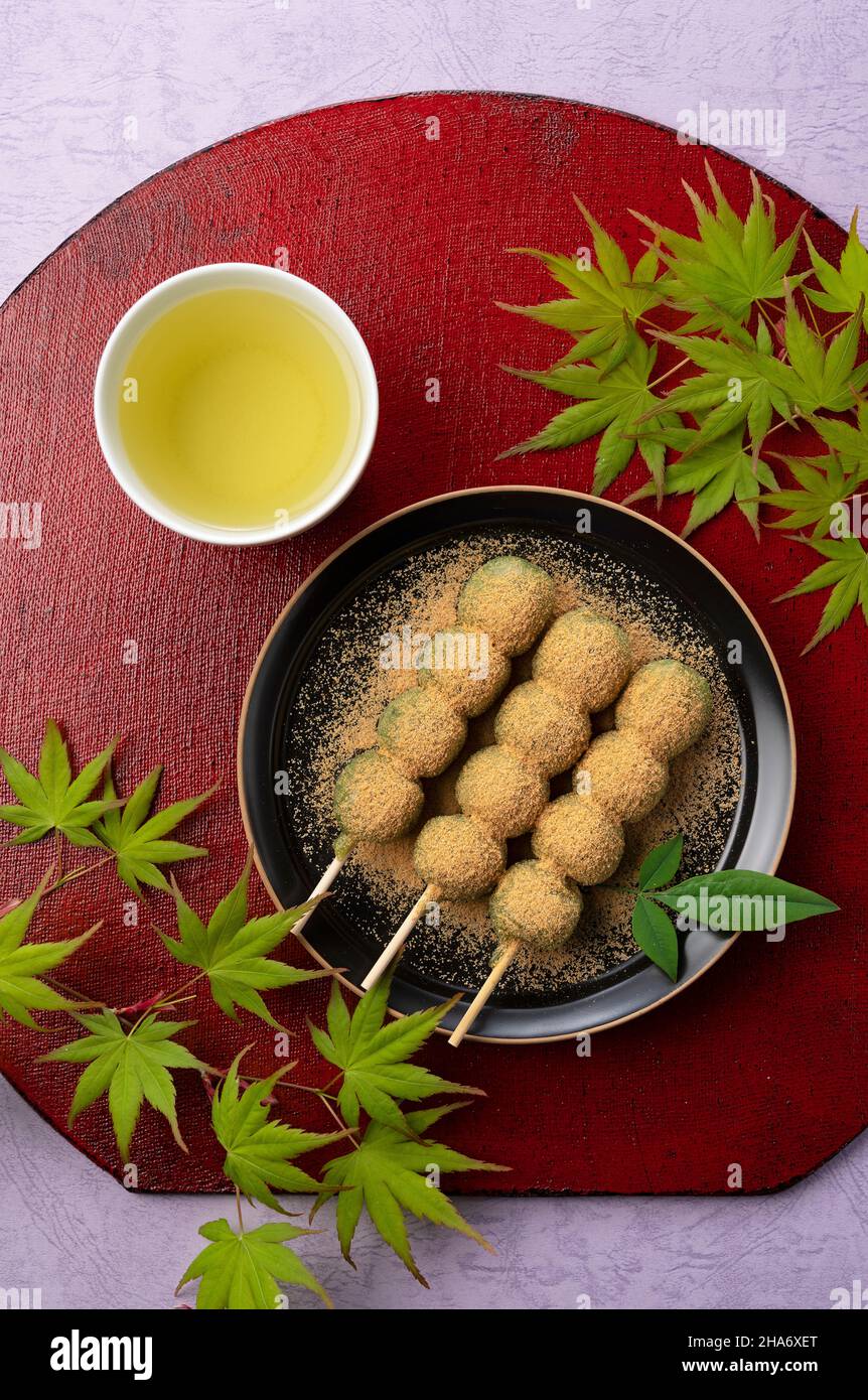 Grass dumplings and green tea served on a black plate placed on a red ...