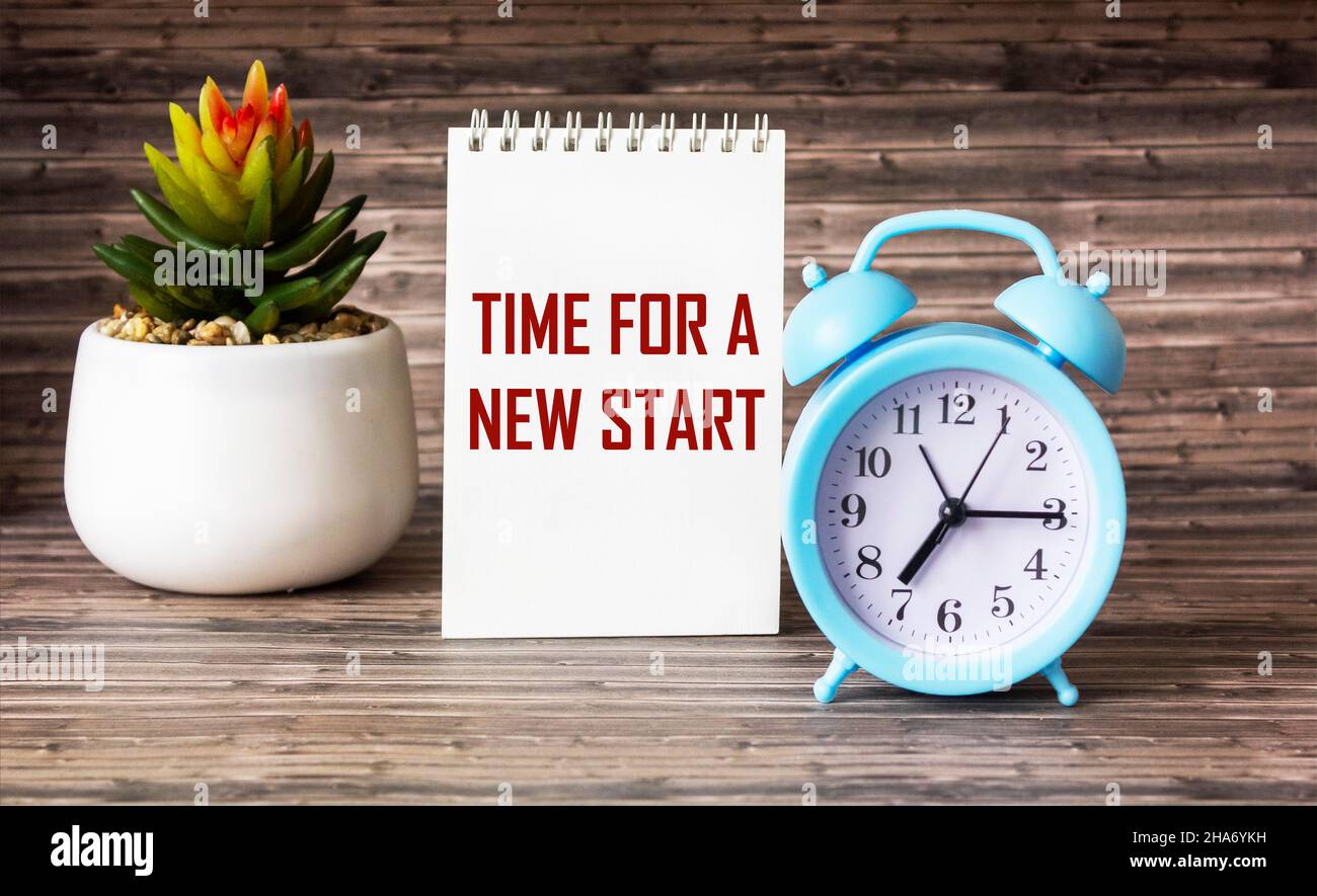 TIME FOR A NEW START text on notepad and wooden background with clock ...