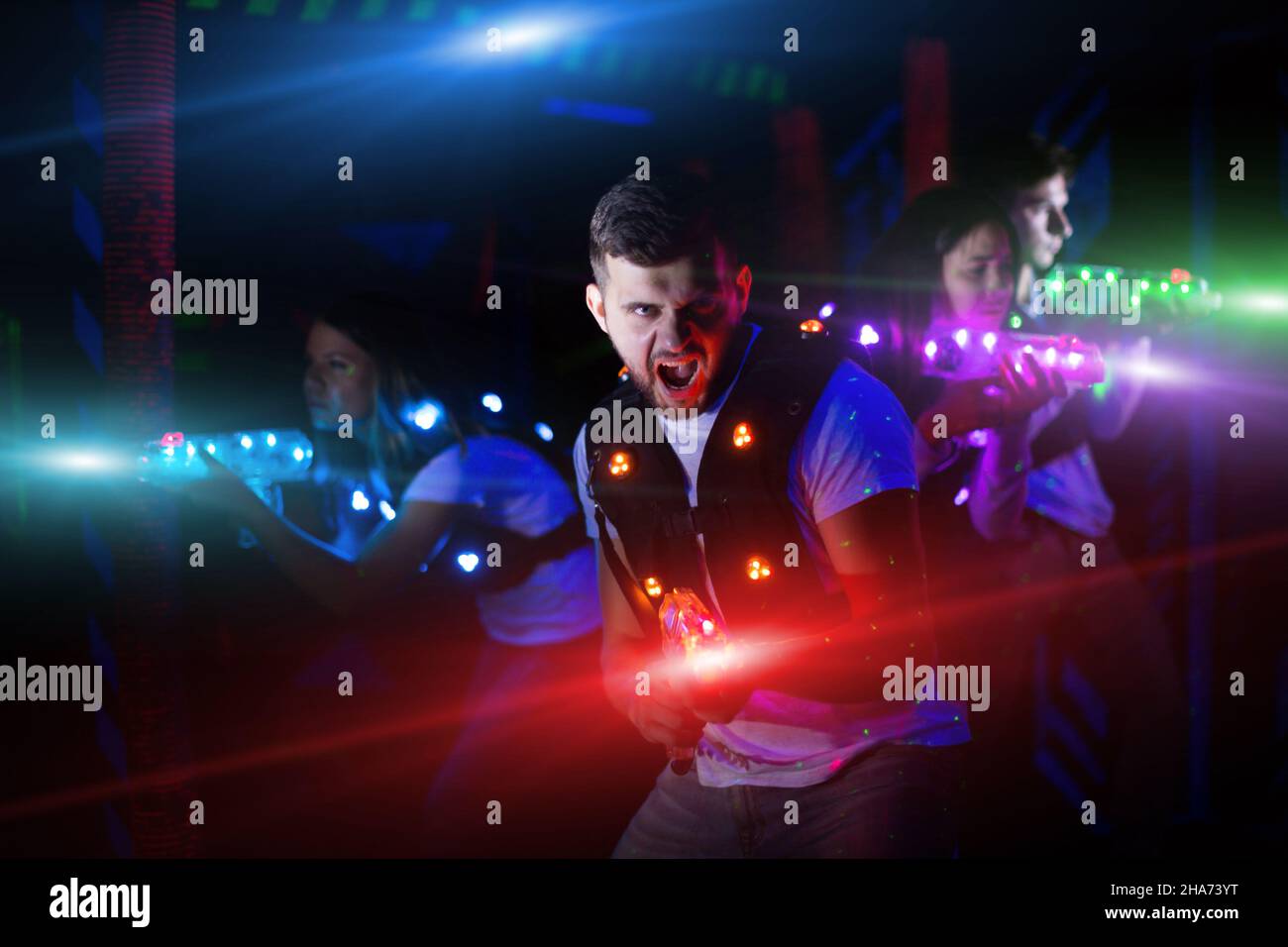 Emotional guy playing laser tag with friends on dark labyrinth in ...