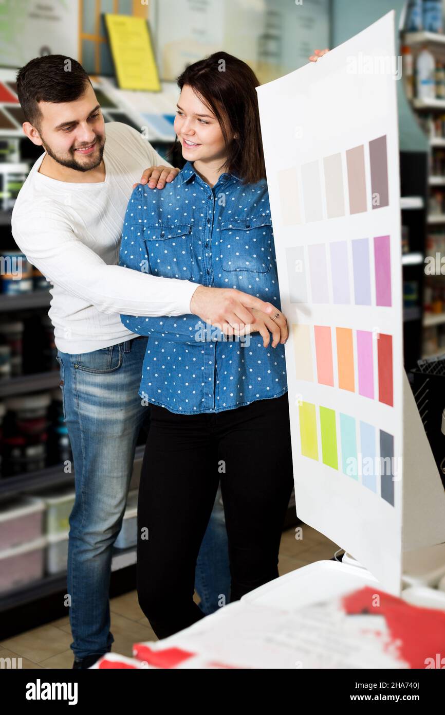 Positive couple examining color scheme variants in paint supplies store ...