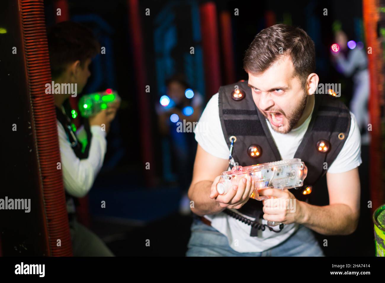 Portrait of young man with laser gun having fun on dark laser tag arena ...