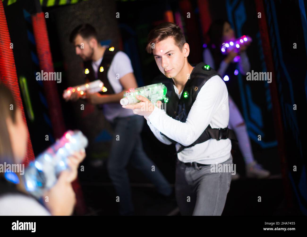 Emotional guy with laser pistol playing laser tag with friends on dark ...