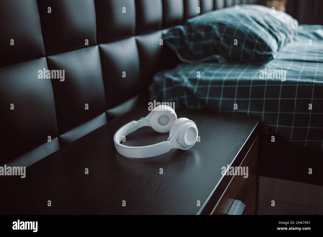 Wireless white headphones lie on the bedside table in the bedroom ...
