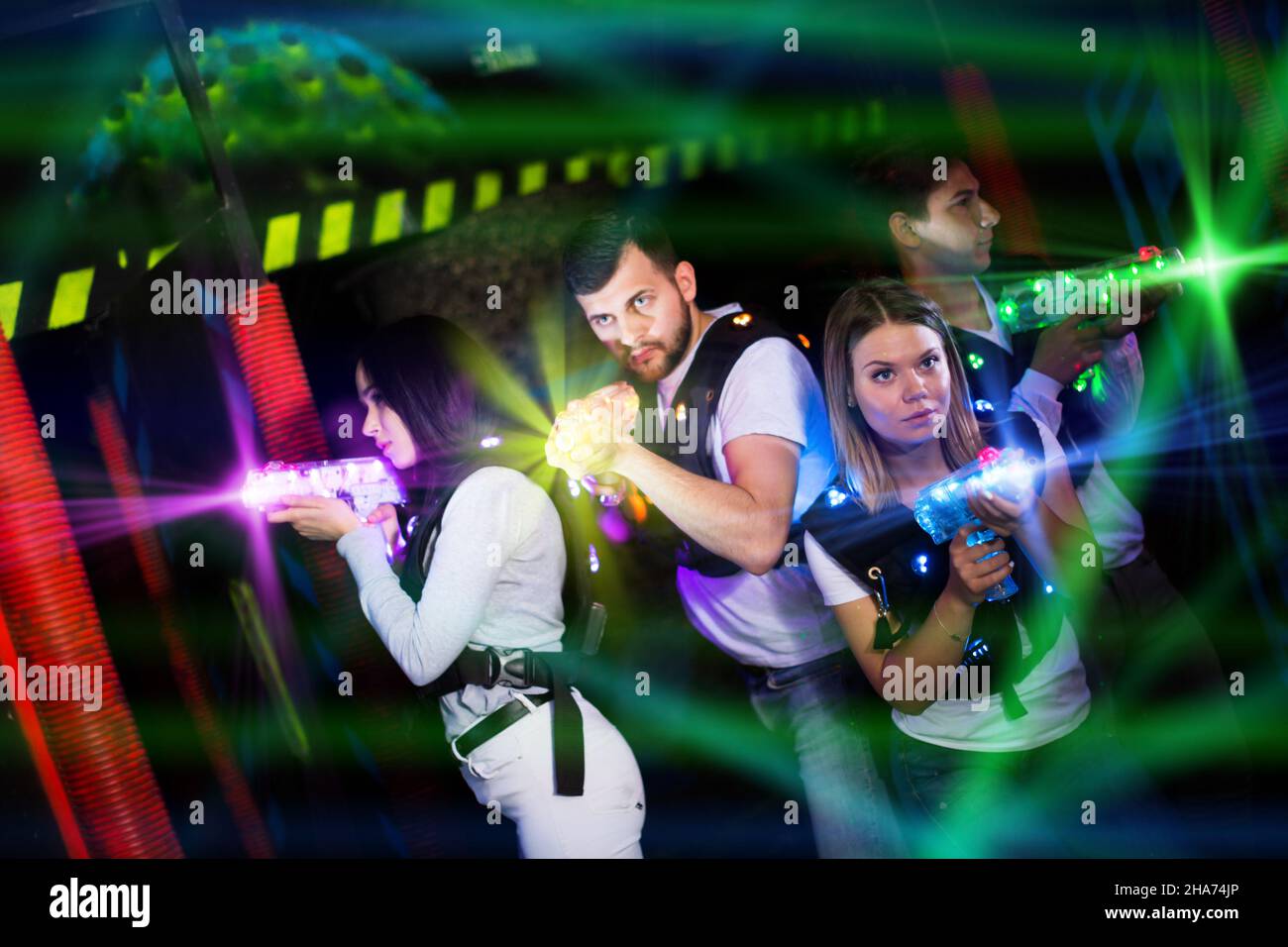 Modern young people playing laser tag on dark labyrinth in bright beams ...