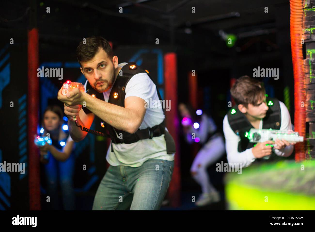 Emotional guy with laser pistol playing laser tag with friends on dark ...