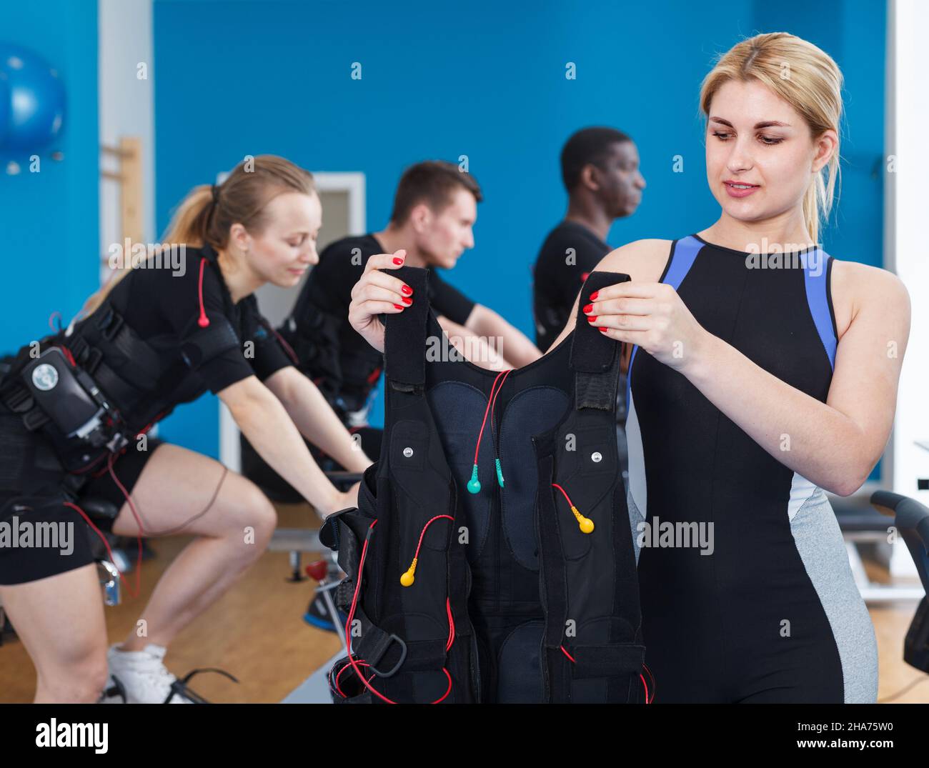 Sporty girl trying on special vest with electrodes for electric muscle ...