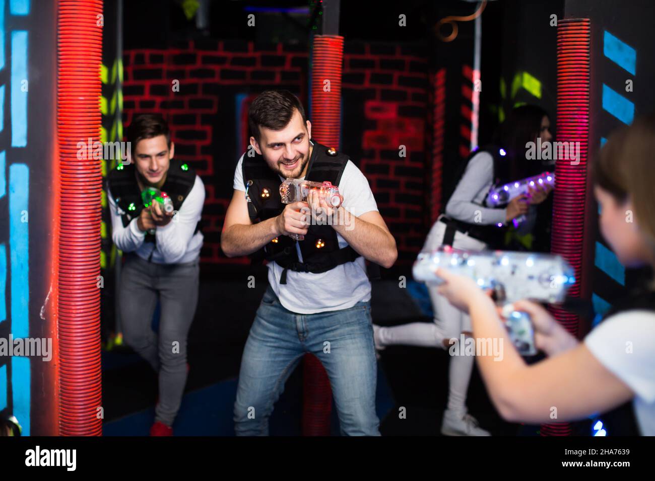 Emotional guy with laser pistol playing laser tag with friends on dark ...