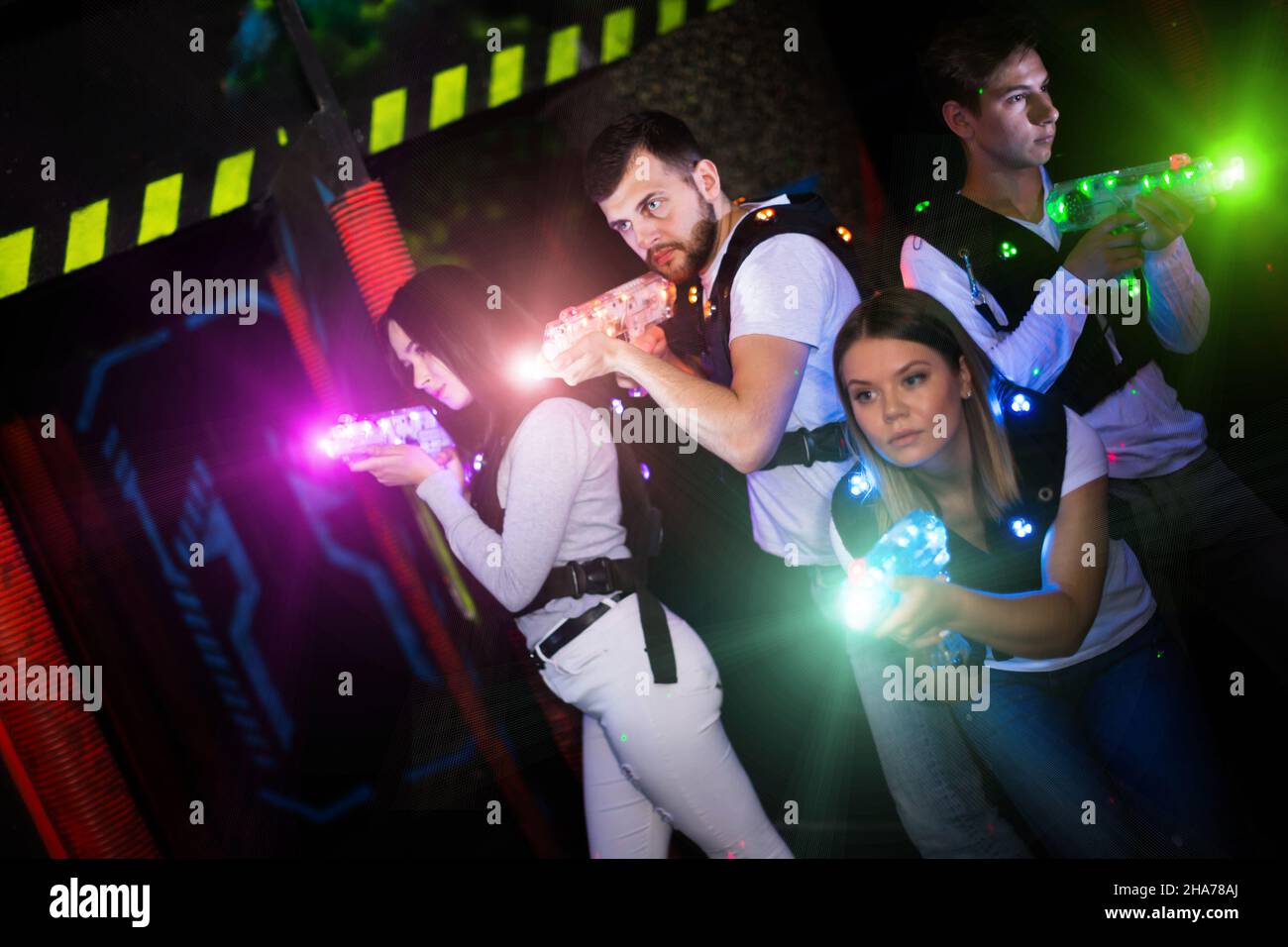 Excited young people in bright beams of laser guns during laser tag ...