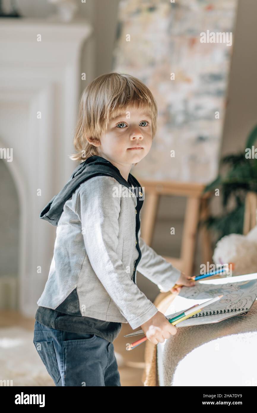 Child toddler blond kid stand draw with pencils inside house, vertical ...