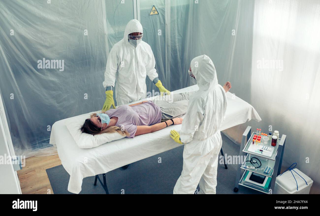 Doctors in bacteriological protection suit observing a patient lying on ...