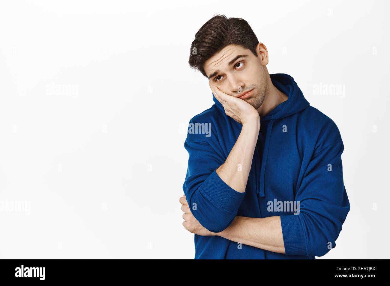 Bored and unamused brunette guy leaning on palm hand, looking away ...