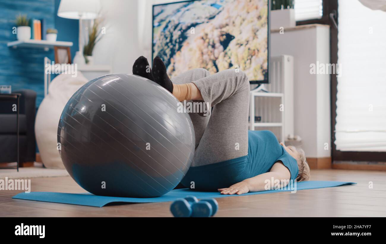 Old woman stretching legs muscles on fitness toning ball to exercise on ...