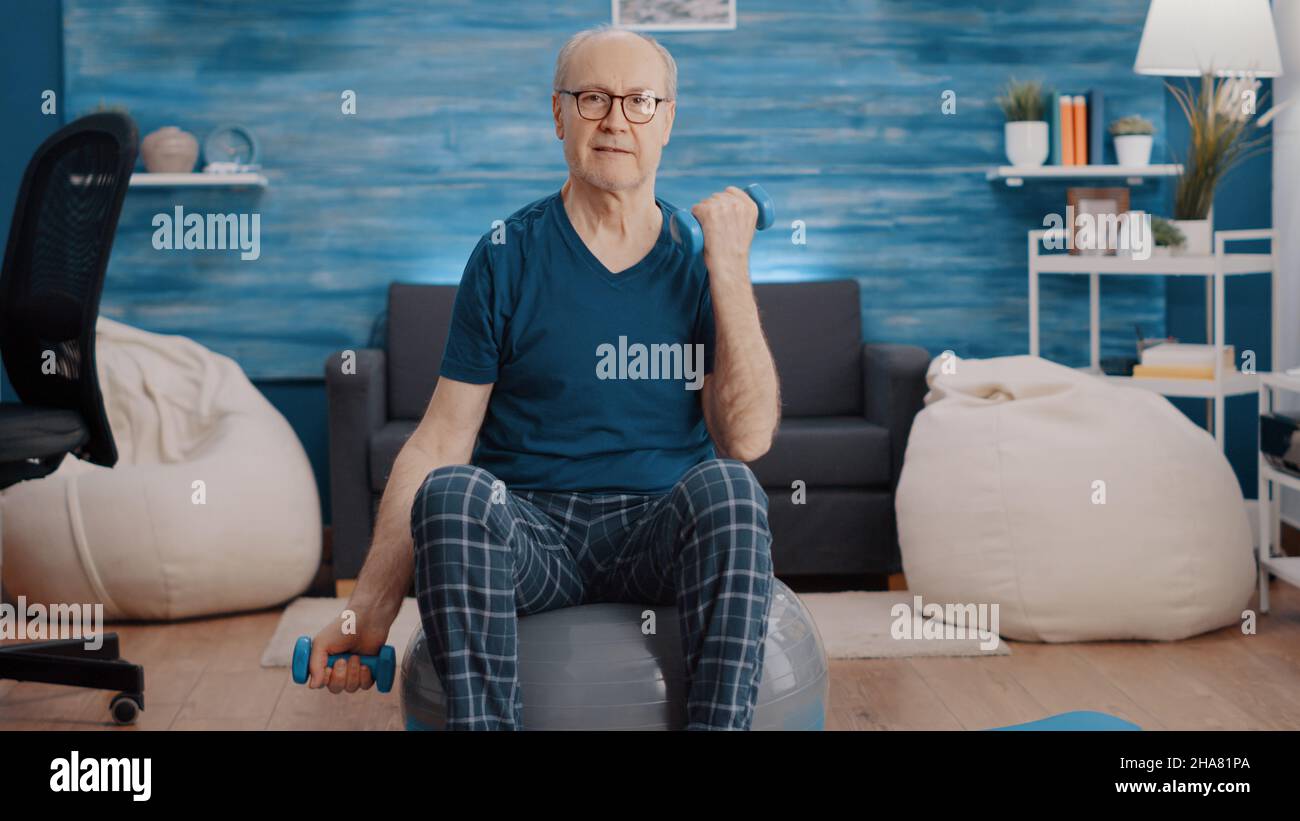 Portrait of senior man sitting on fitness toning ball and using ...