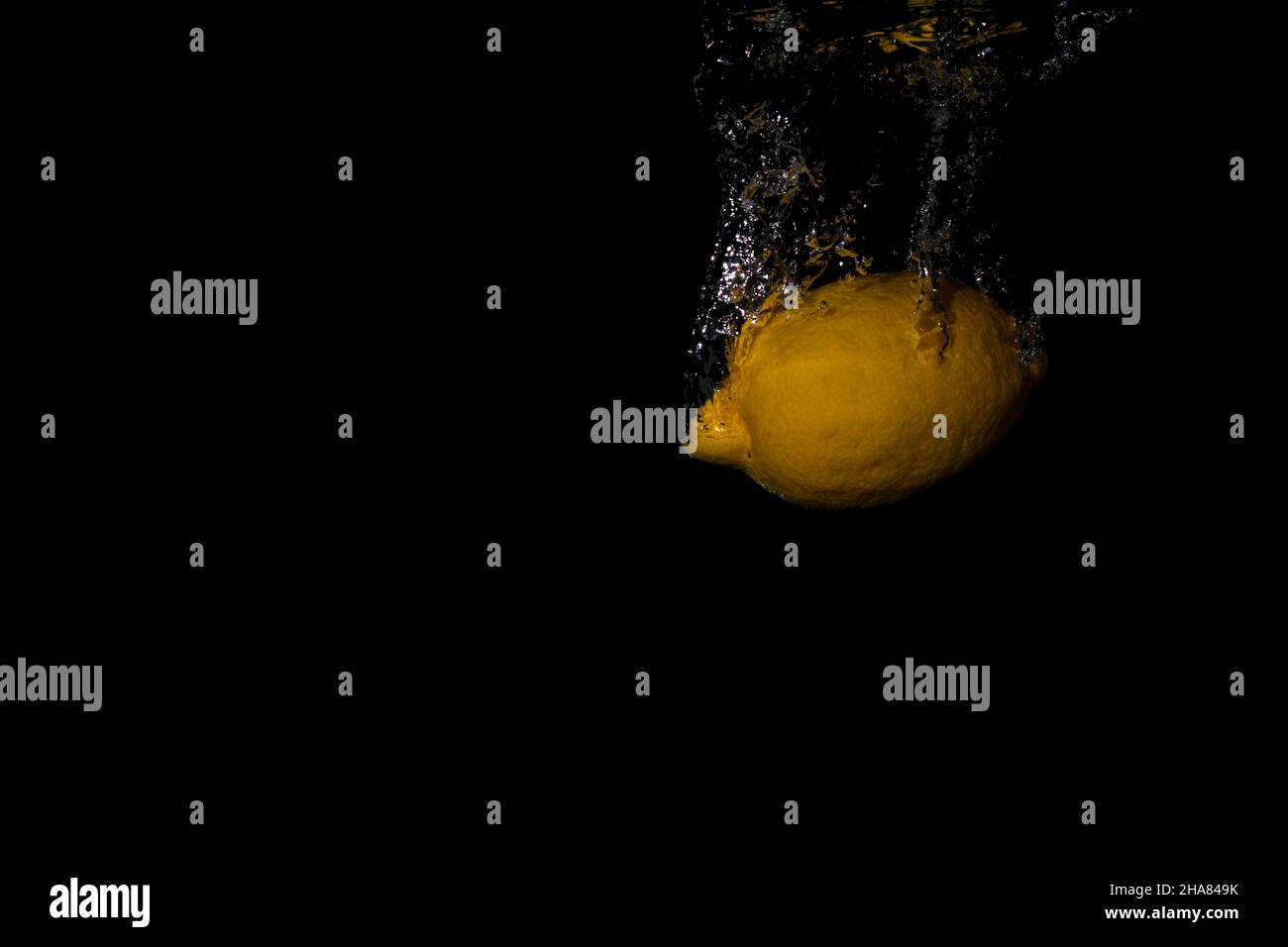 Closeup shot of lemon falls into the water with air bubbles and ...