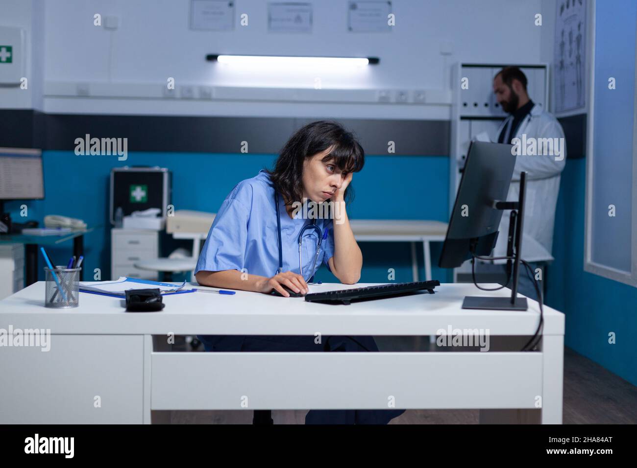 Sleepy nurse looking at computer screen for healthcare at office ...
